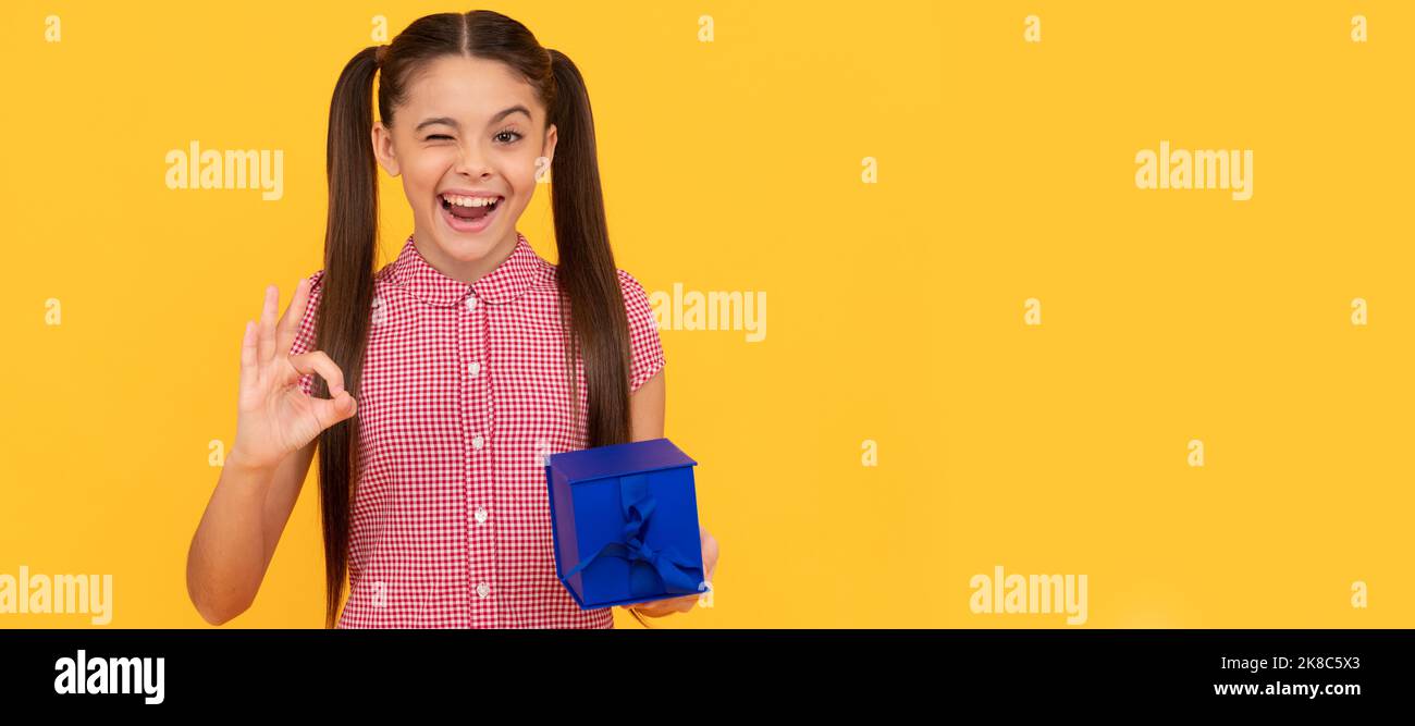 happy kid hold present box on yellow background winking with ok gesture ...