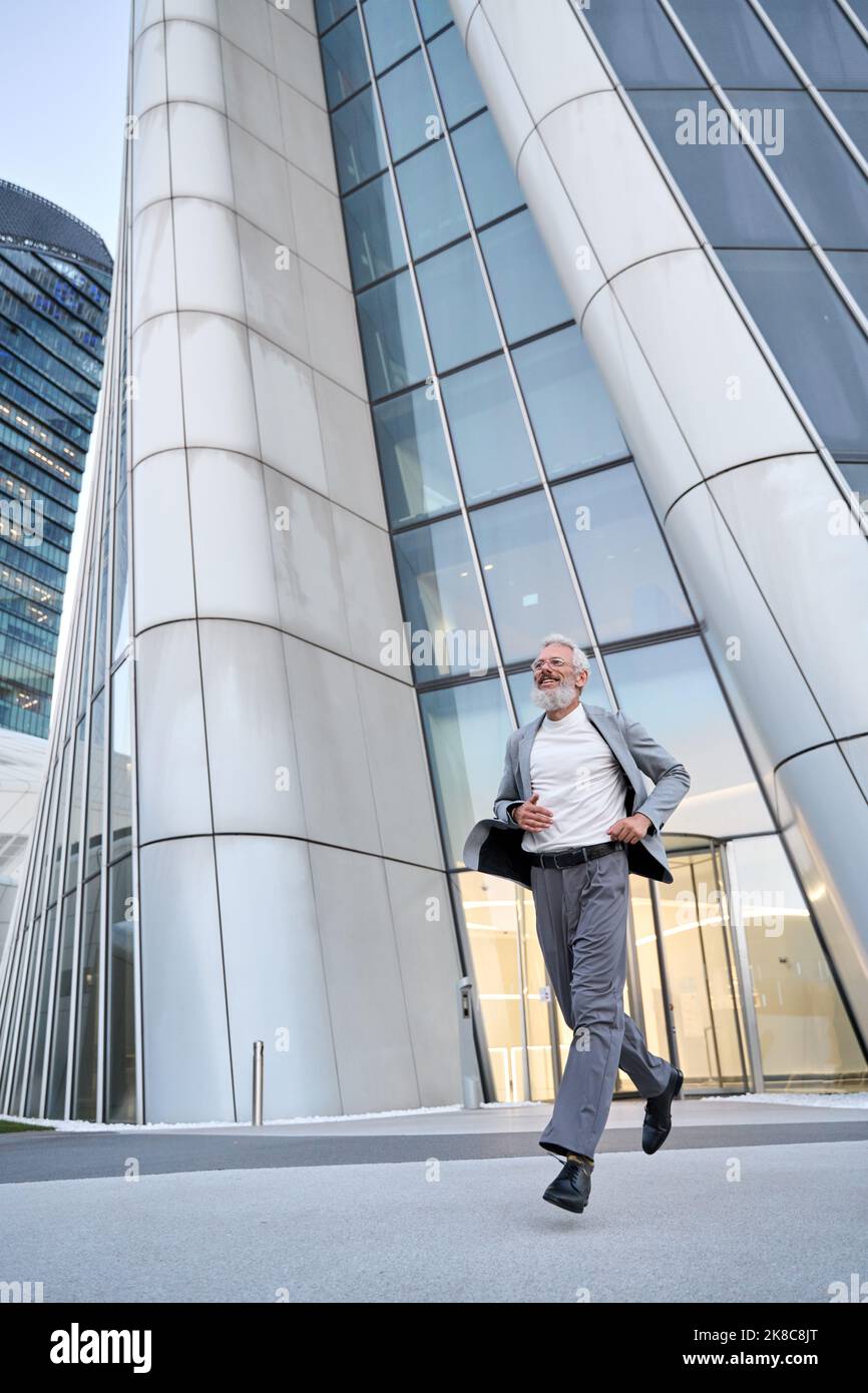 Happy stylish older business man wears suit running outdoor in big city ...