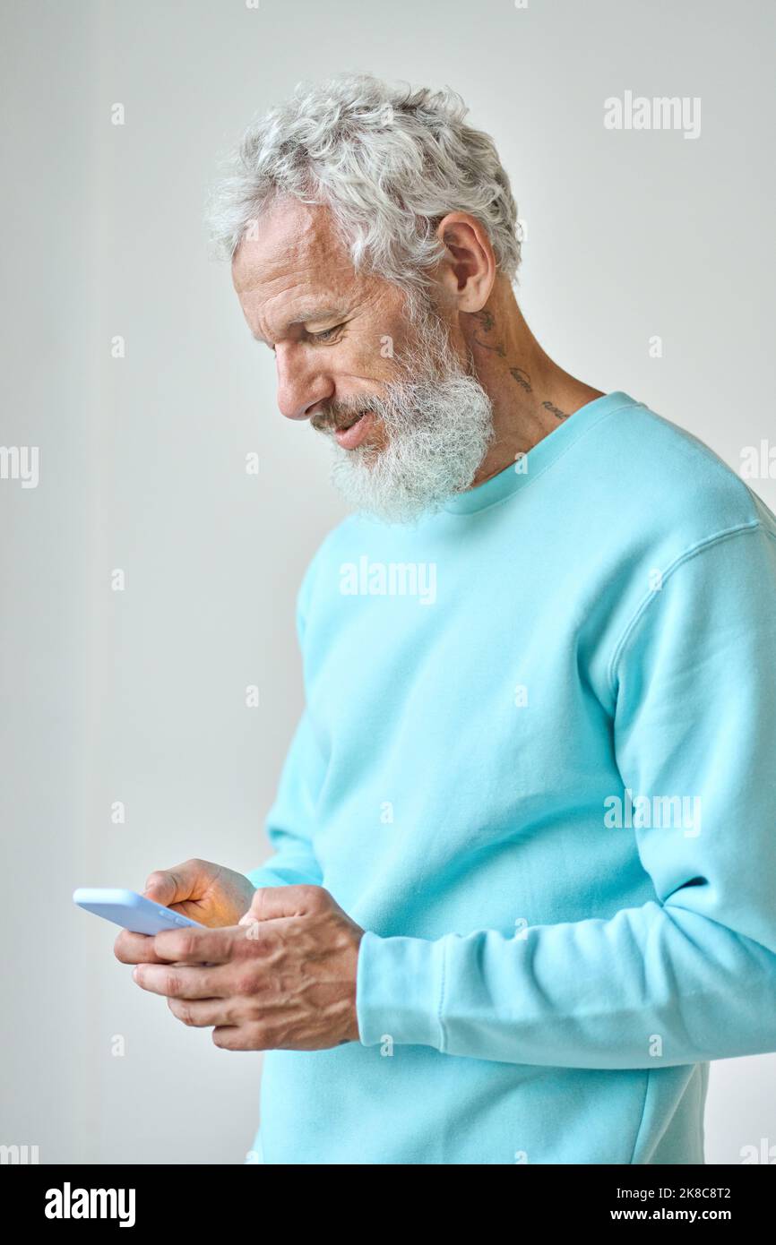 Older senior bearded hipster man using cell phone standing at white ...