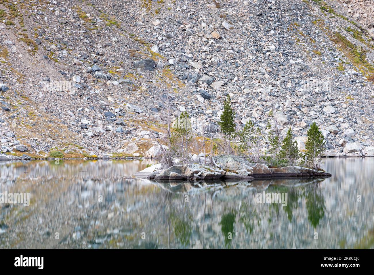 A small island of rocks and trees rising out of the reflective waters ...