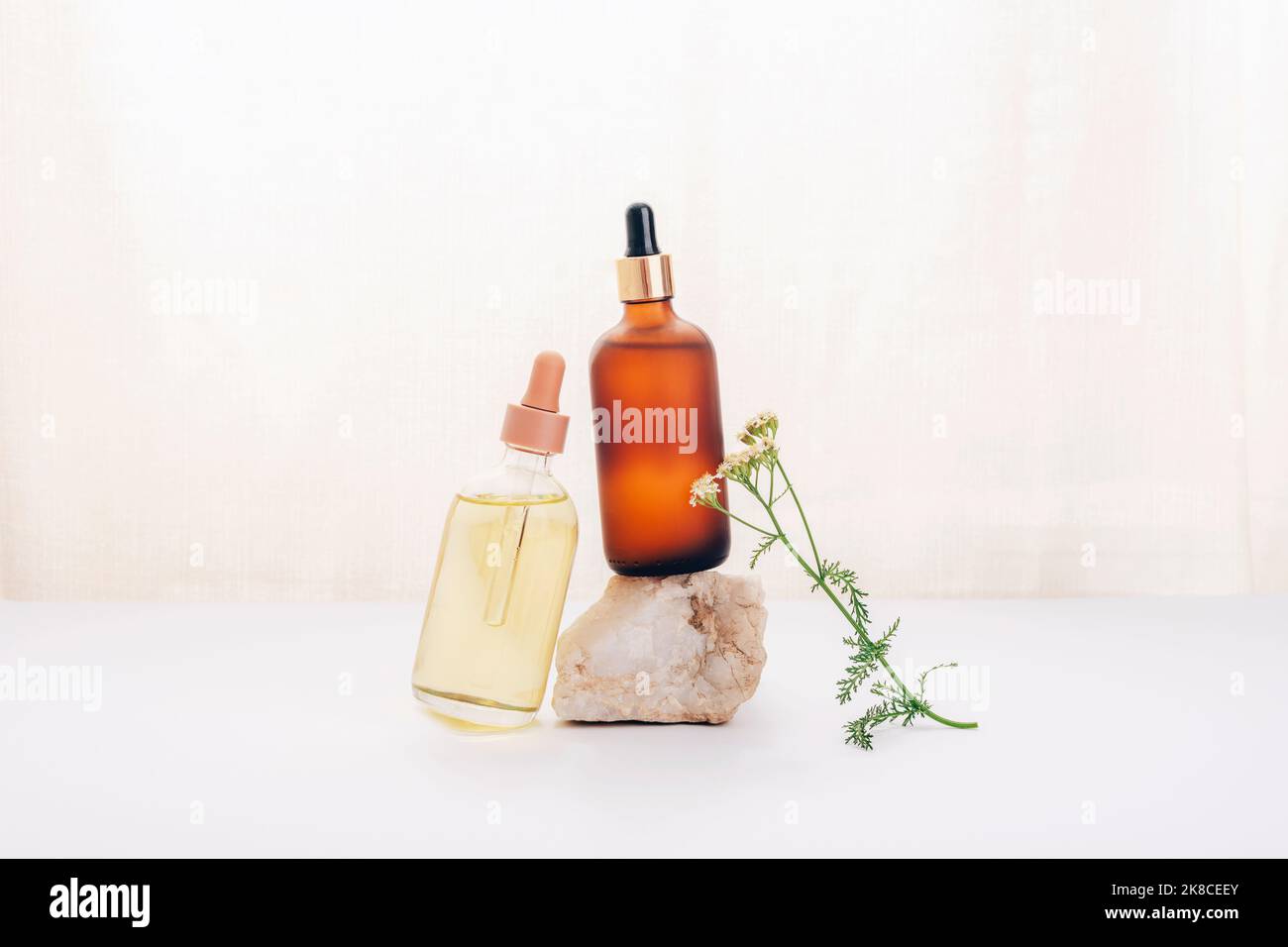 Two cosmetic oil or serum bottles on a stone and yarrow flower on white ...