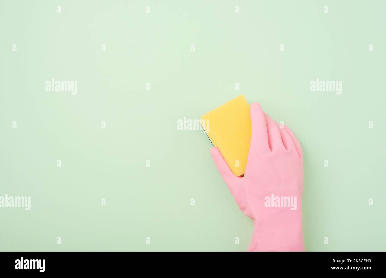 Hand in pink rubber glove holding yellow sponge on light green ...