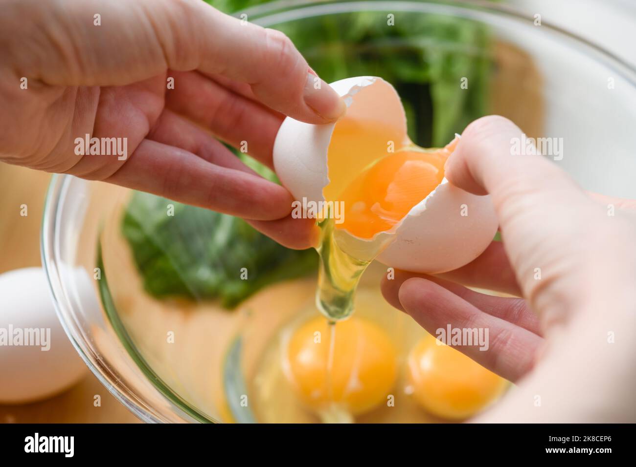 Close-up of a female pair of hands cracking an egg in a glass bowl ...