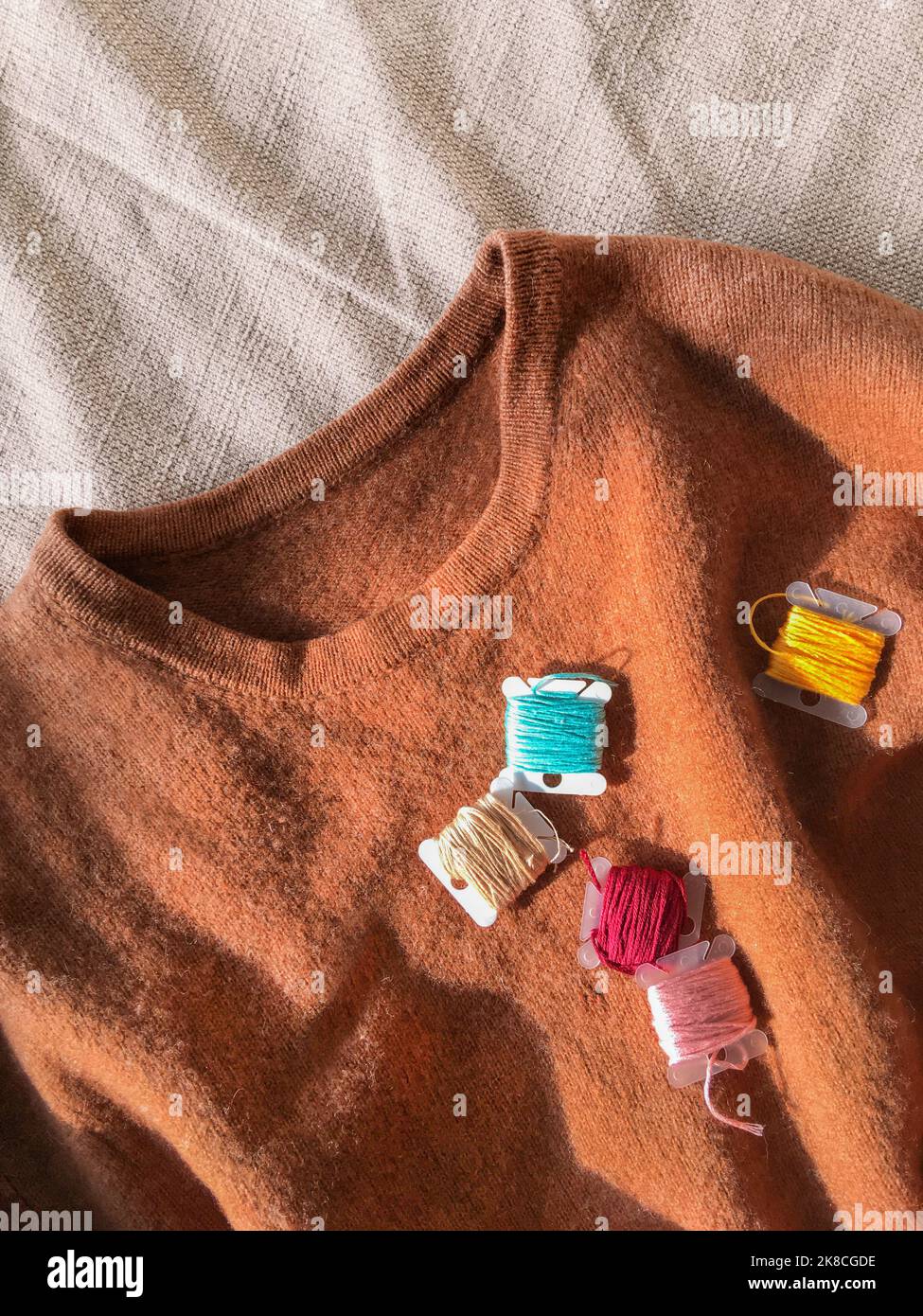 Top view on earth toned wool sweater and coils of colorful embroidery ...