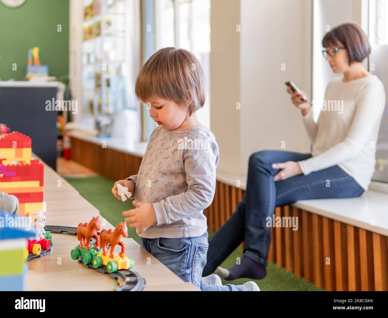 Toddler plays with colorful toy blocks while his mother or babysitter ...
