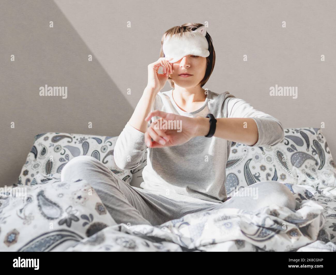 Sleepy woman in grey pajama and sleeping mask on face. She is just woke ...