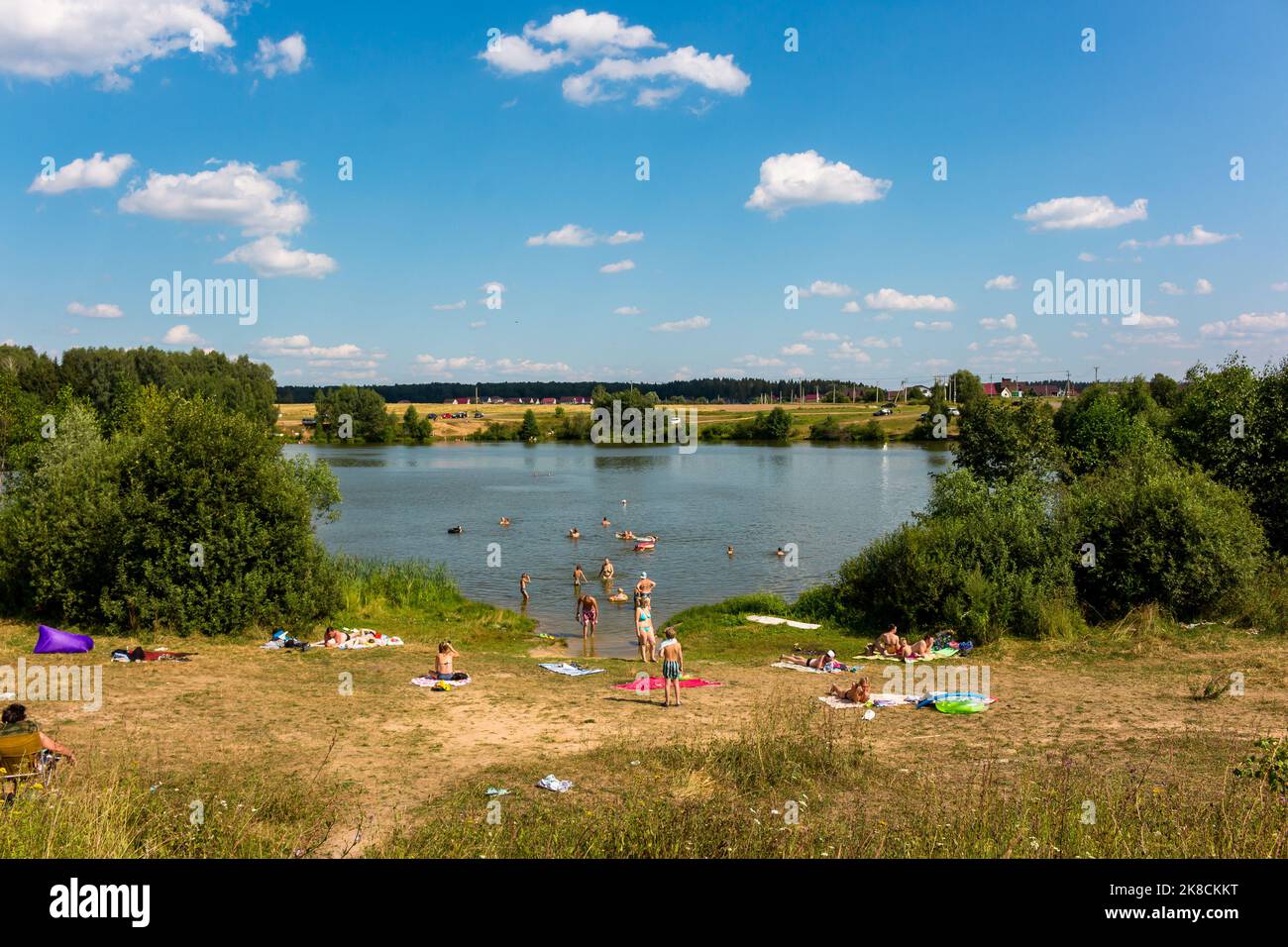 A simple wild beach on a small rural lake, people swim in a pond on a ...