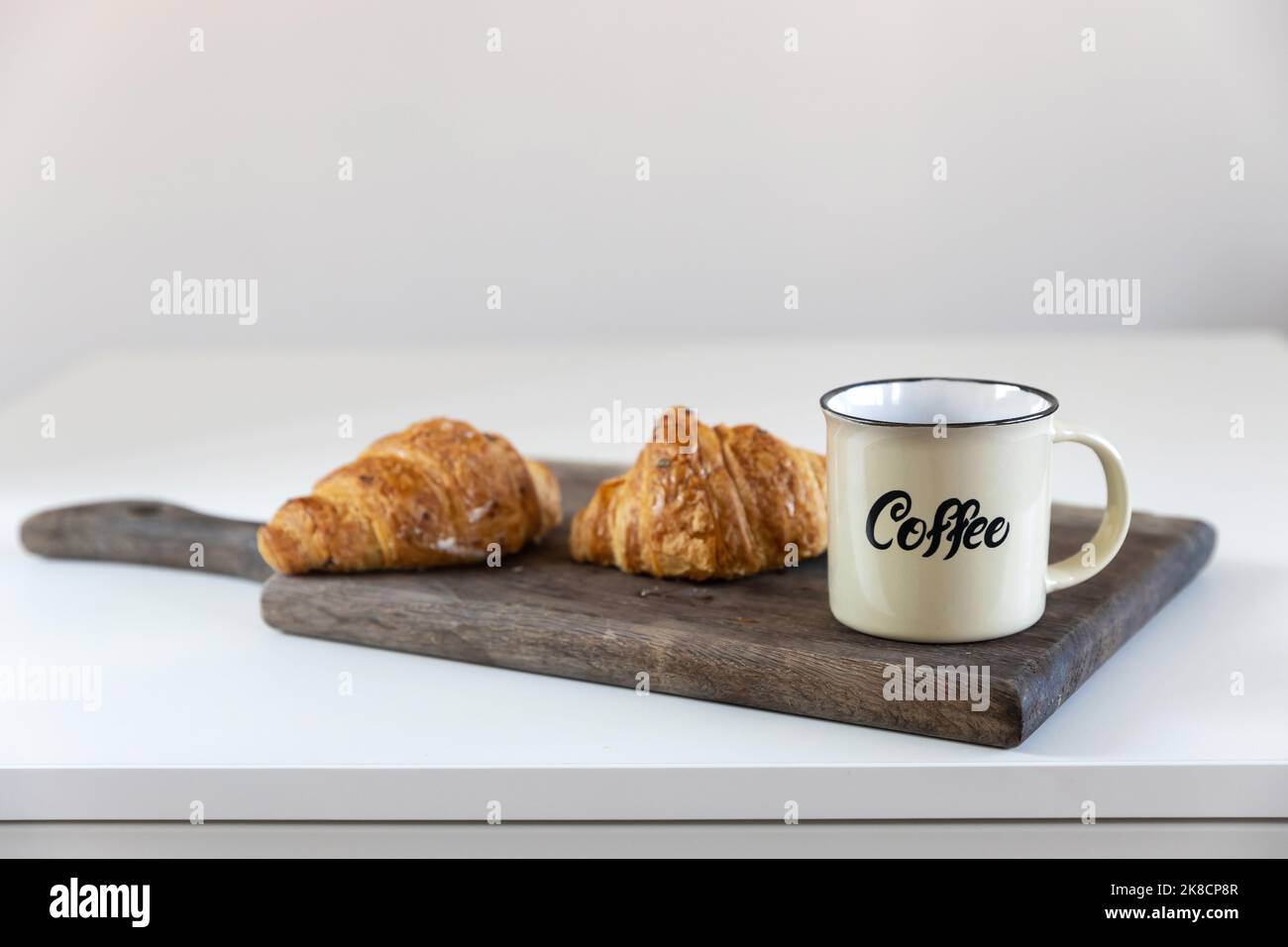Two croissants, a cup with coffee inscription on a wooden board on a ...