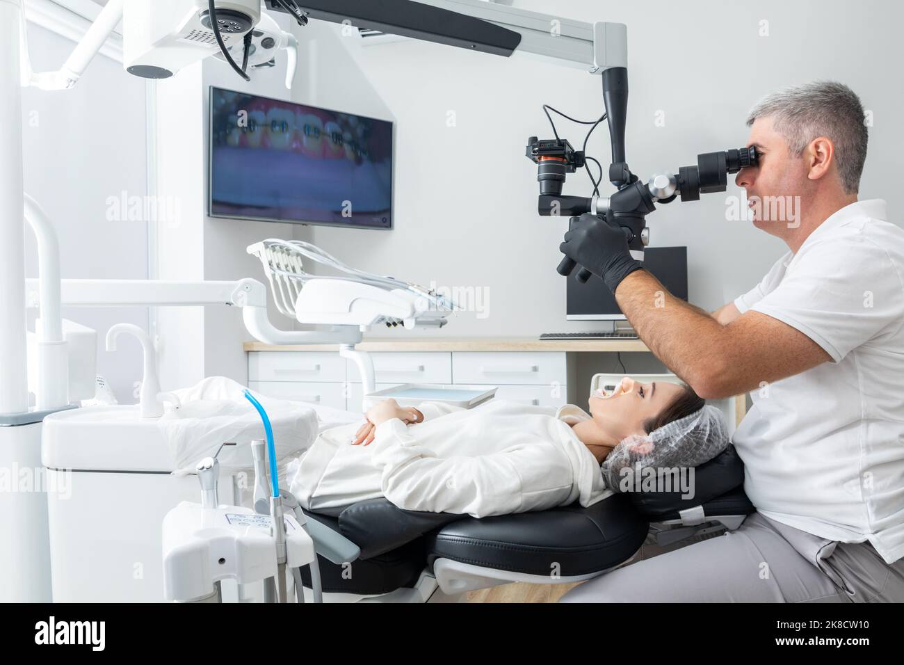 Dentist using dental microscope treating patient teeth at dental clinic ...