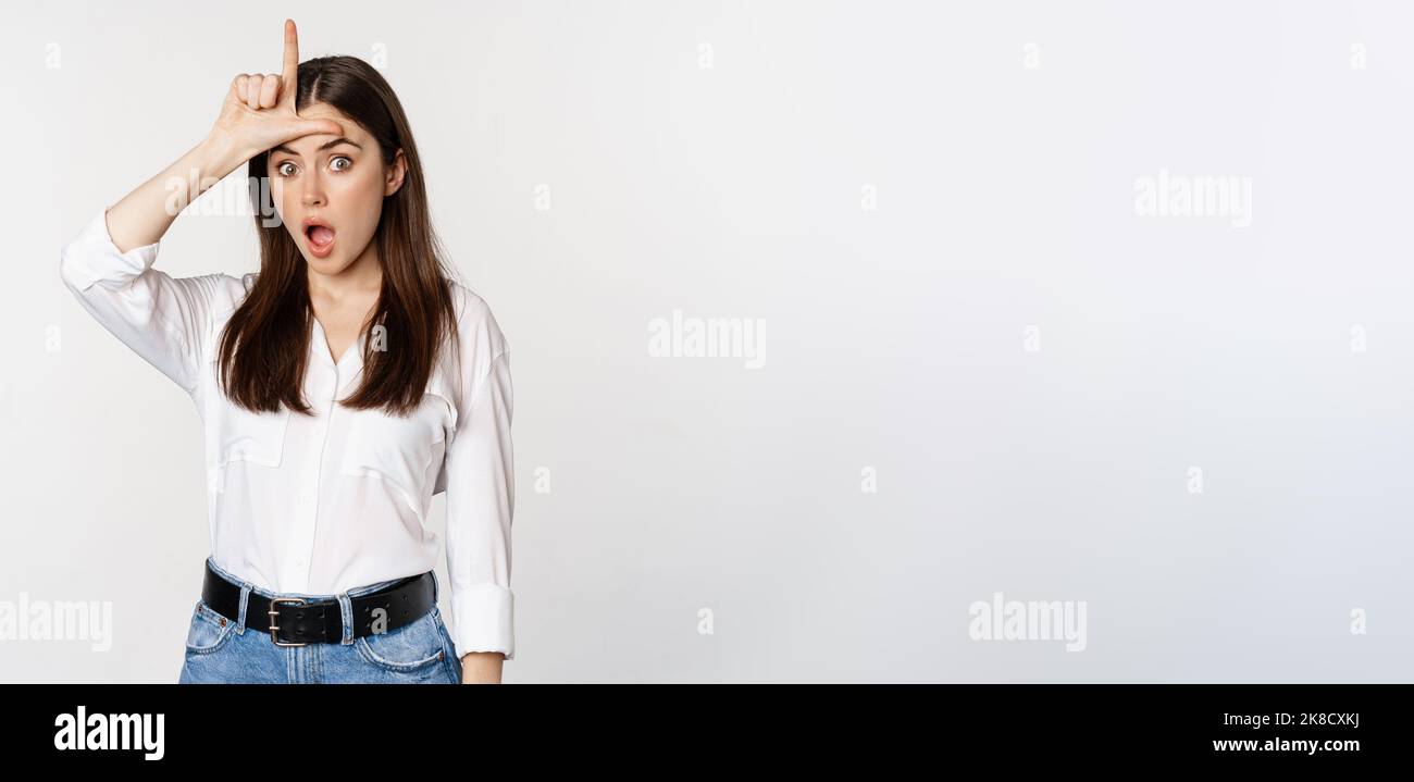 Young woman mocking loser, showing L word sign on forehead and gasping ...