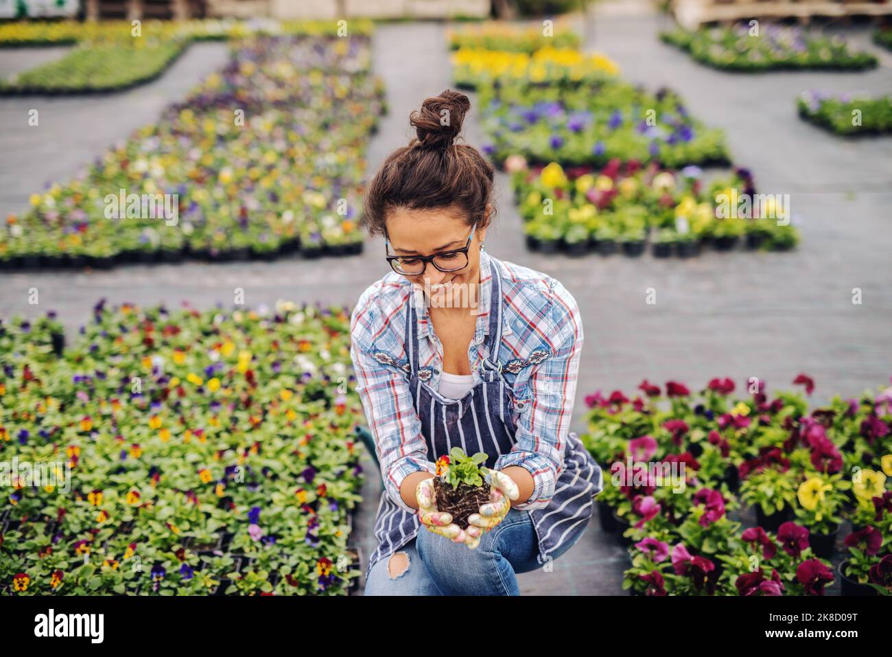 Cute smiling florist crouching outdoors surrounded by flowers and ...
