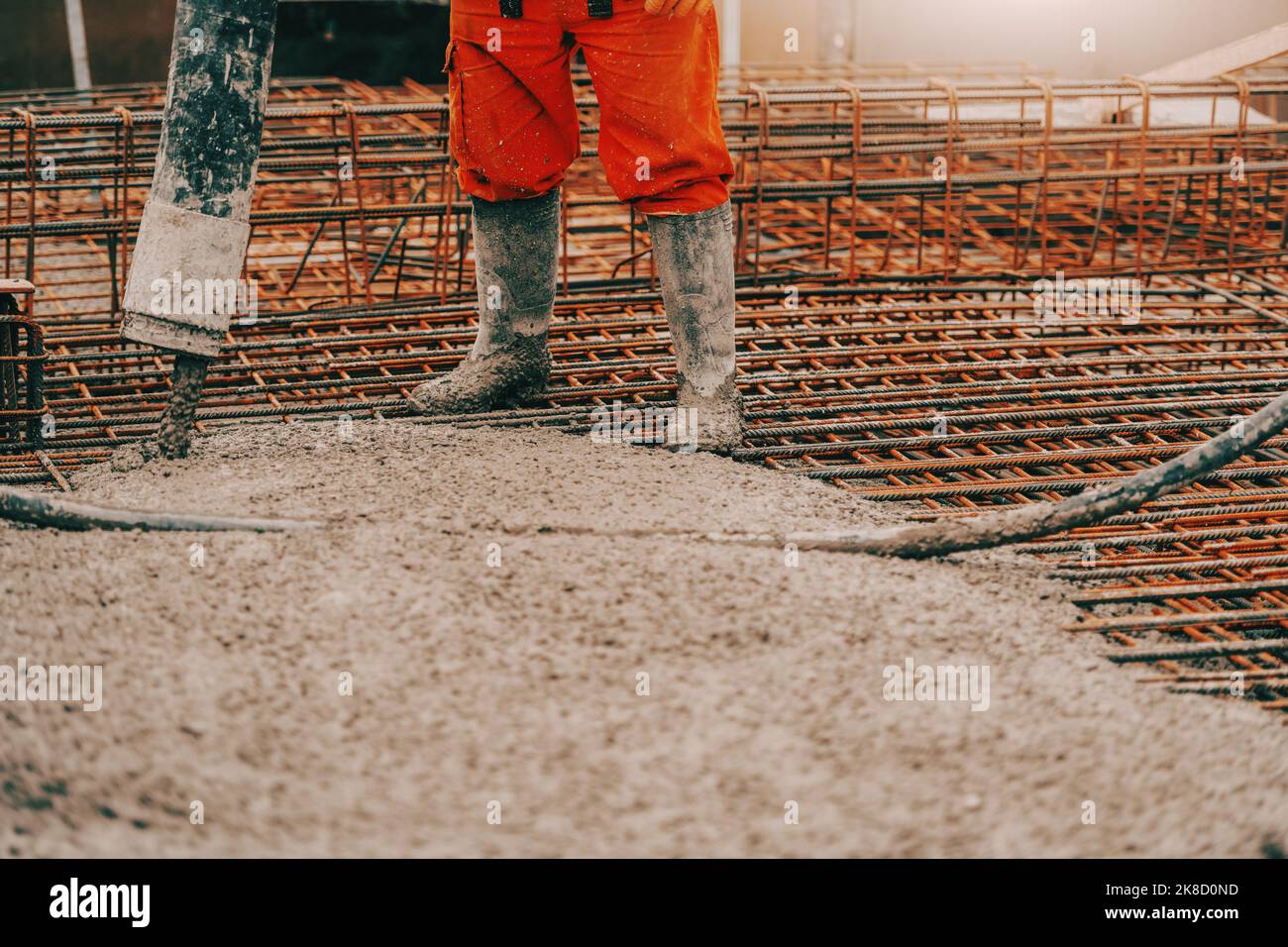 Construction site worker in boots and orange protective suit pouring ...