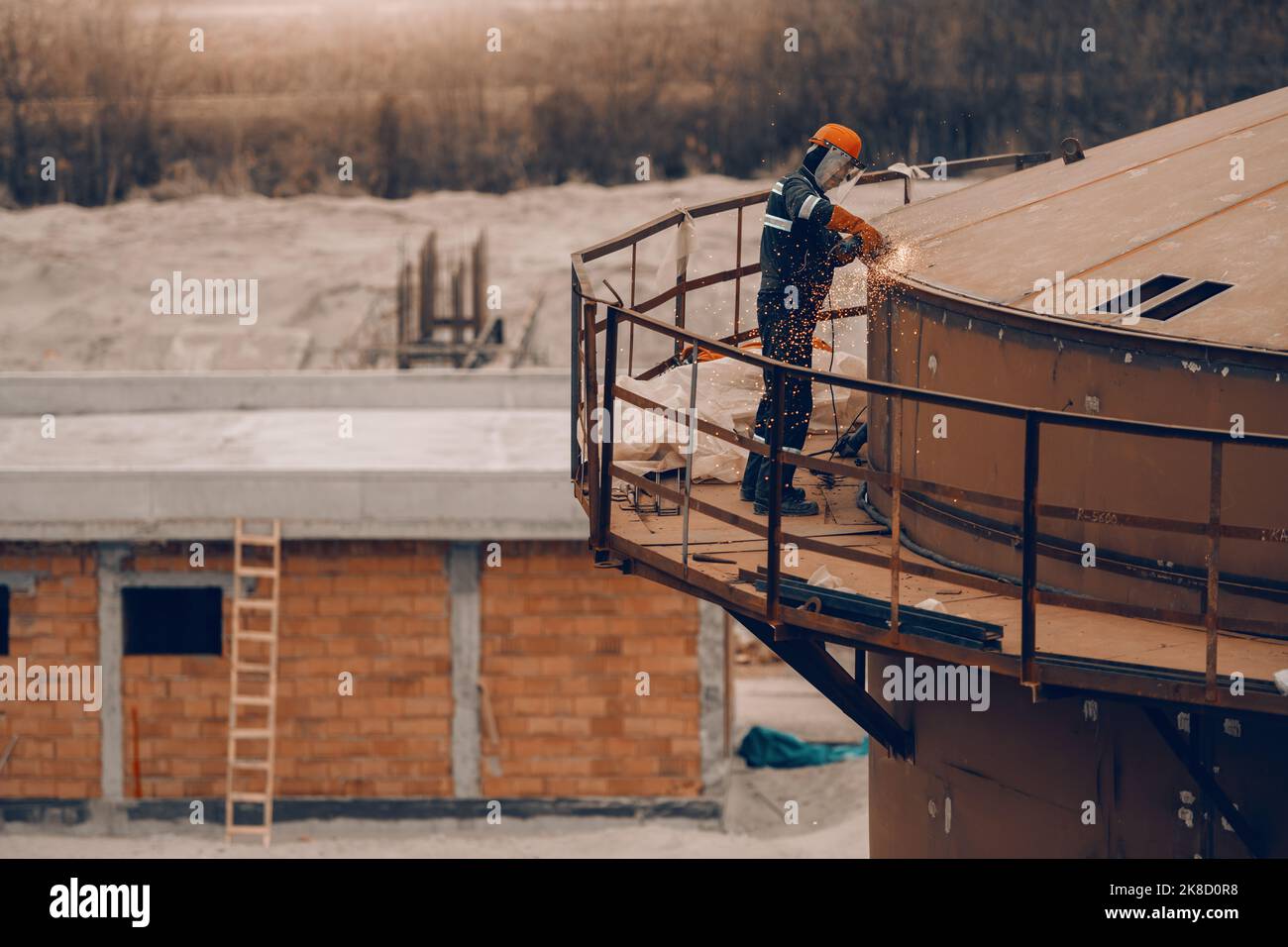 Worker in protective uniform and helmet grinding top of tower on ...