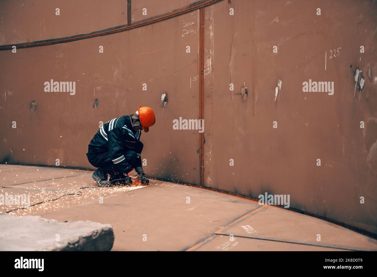 Worker in protective suit and helmet crouching and grinding in metal ...