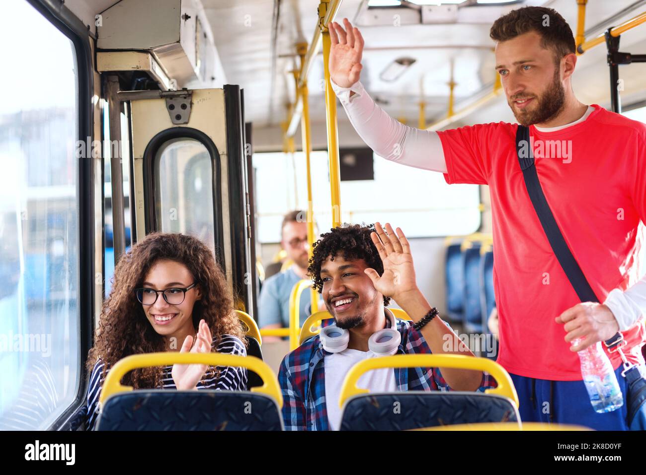 Happy multicultural friends waving to someone while sitting and ...