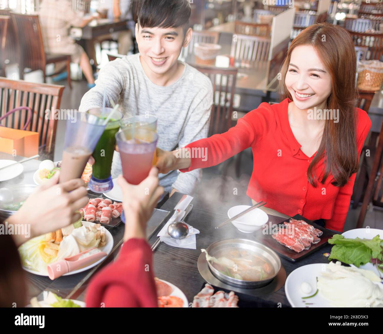 Happy Young people toasting and having dinner in hot pots restaurant ...