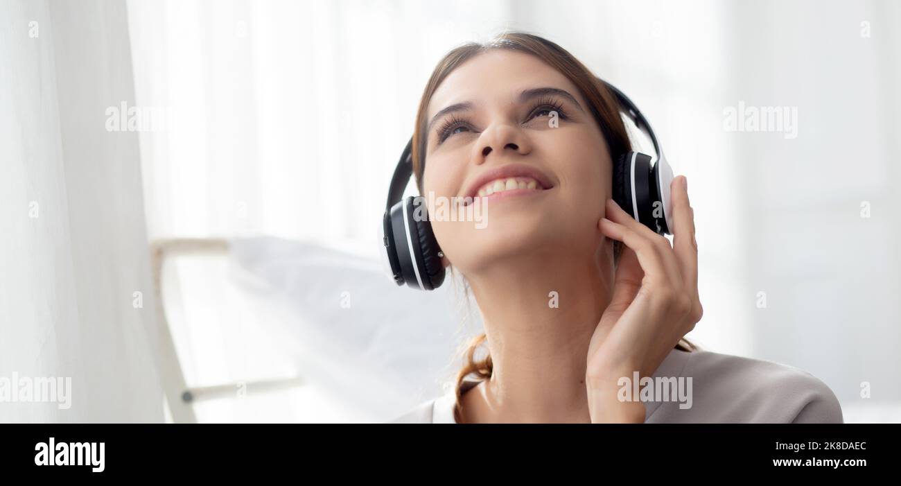Happy young woman wearing headphones listening music while using laptop ...