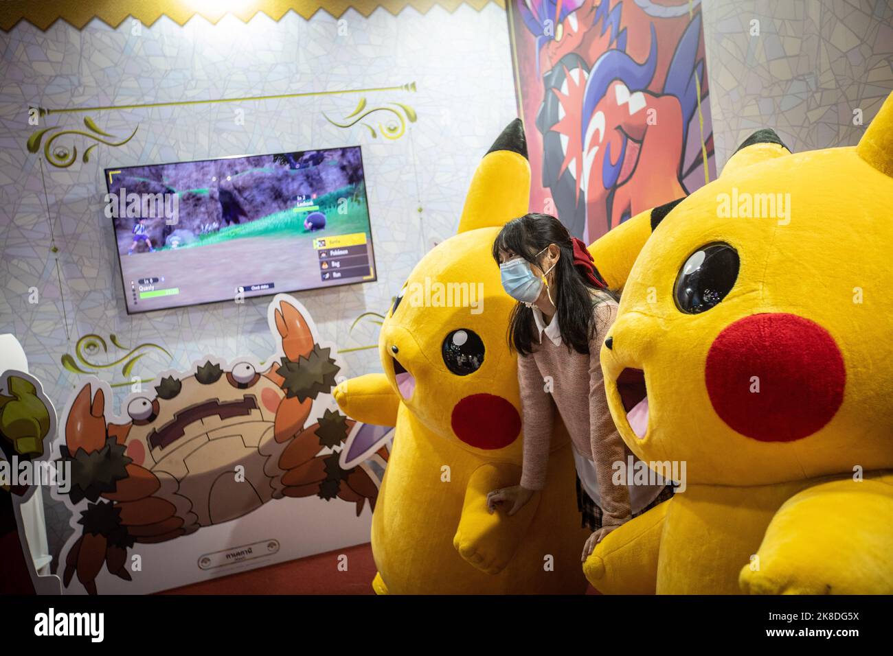 A visitor poses for a picture with two Pikachu mascots at the Pokemon ...