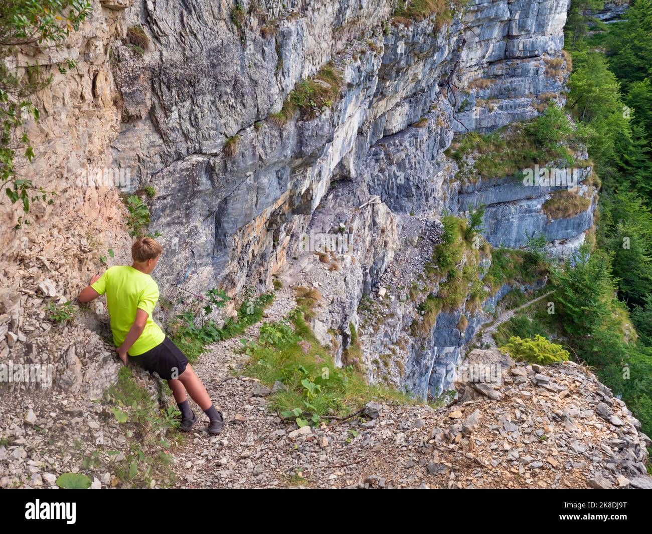 Boy in yellow tshirt looking down from path with steel chain anchored ...