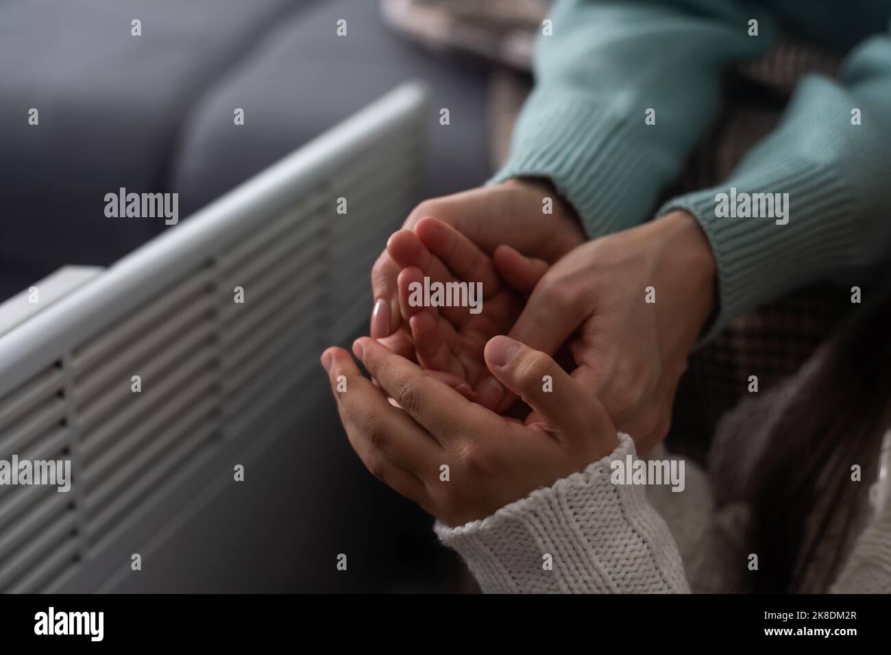 Mother and child warming hands near electric heater at home, closeup ...