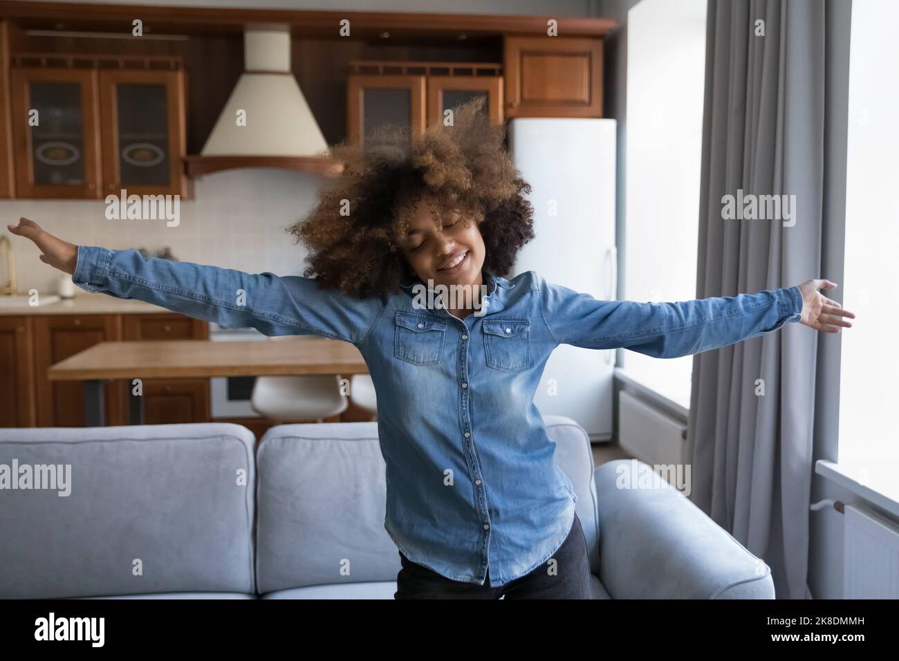 Carefree lively African teenage girl having fun dancing alone indoors ...