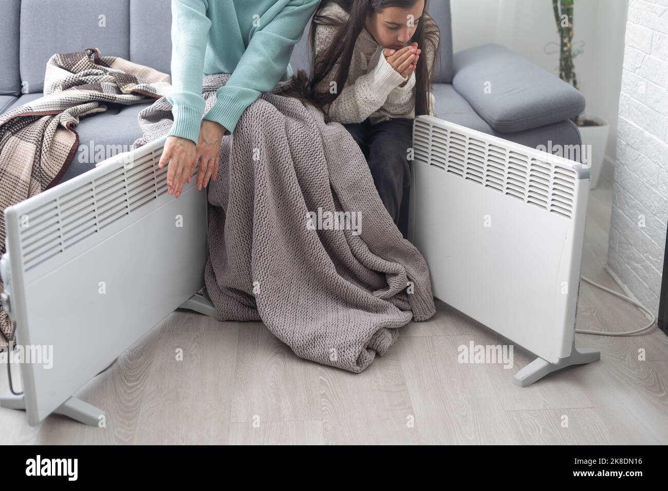 At the electric heater, people are warming themselves, covered with a ...