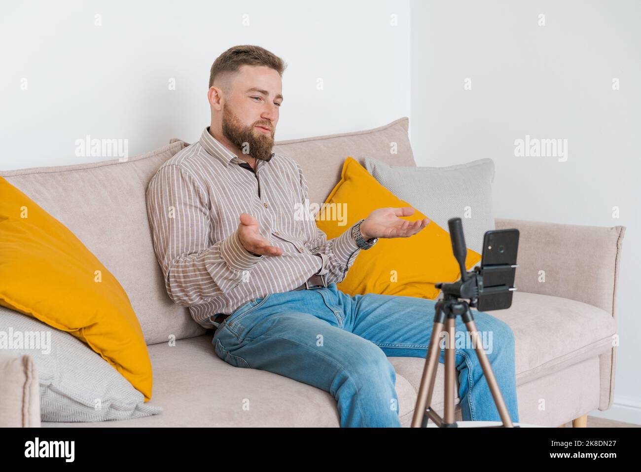 Smiling bearded guy filming video using smartphone on tripod online ...