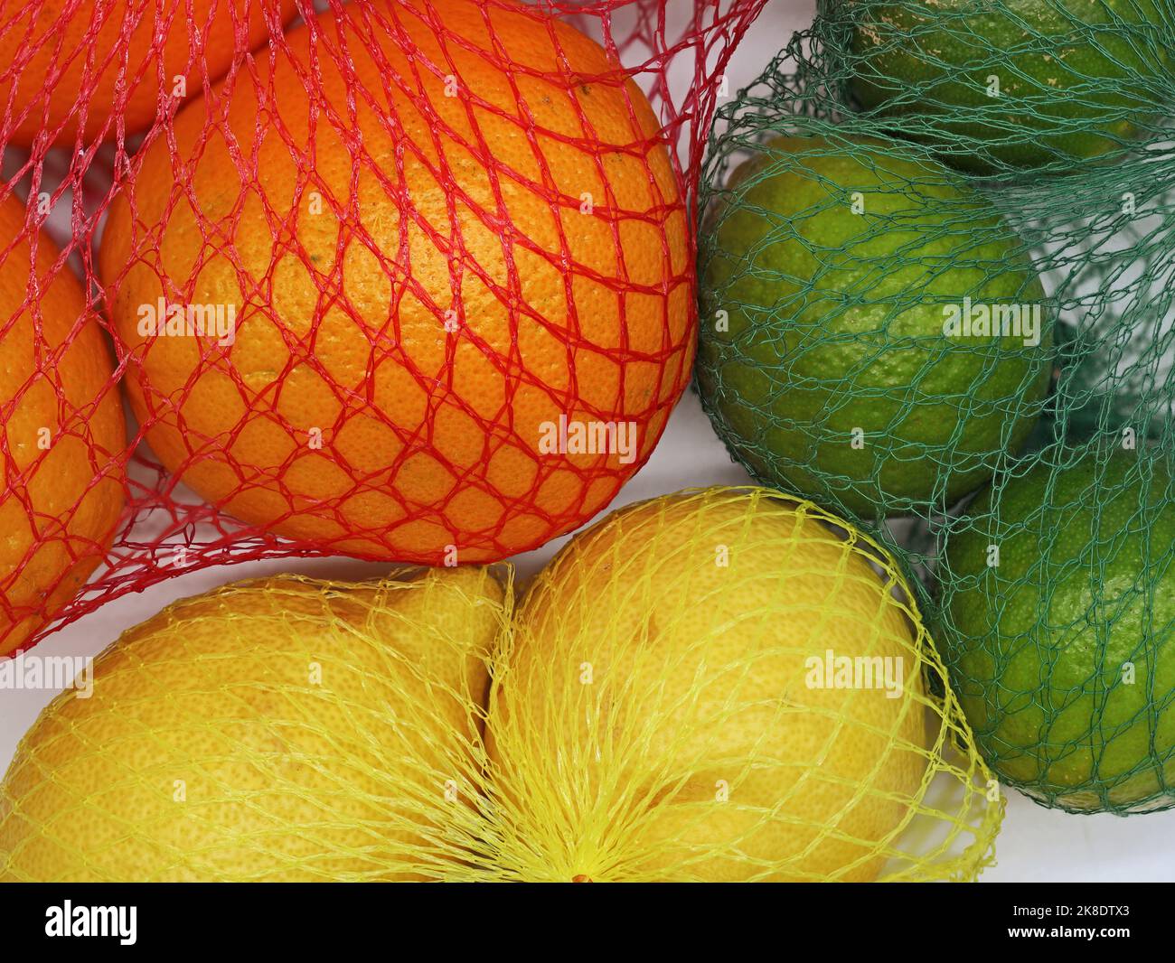oranges, limes and lemons in plastic net bag, close up of citrus fruits ...