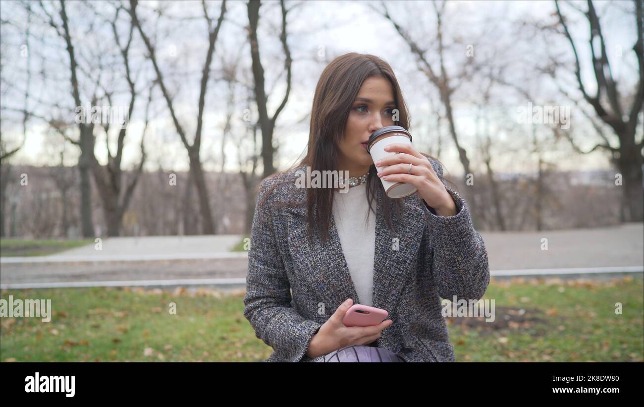 Girl in the park on a bench drinks coffee. Girl sitting on a wooden ...