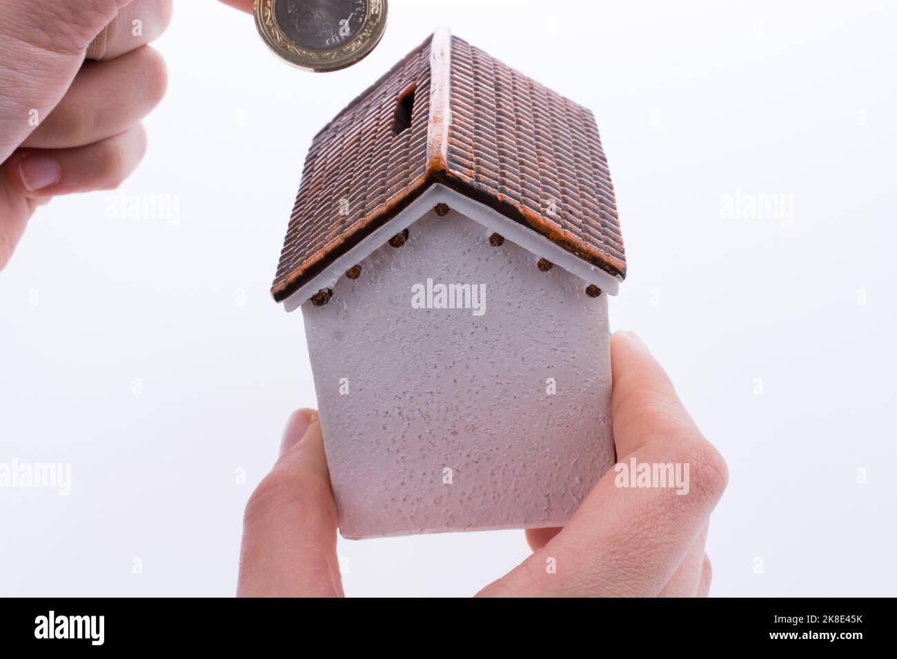 Hand dropping coin into the moneybox in the shape of a model house ...