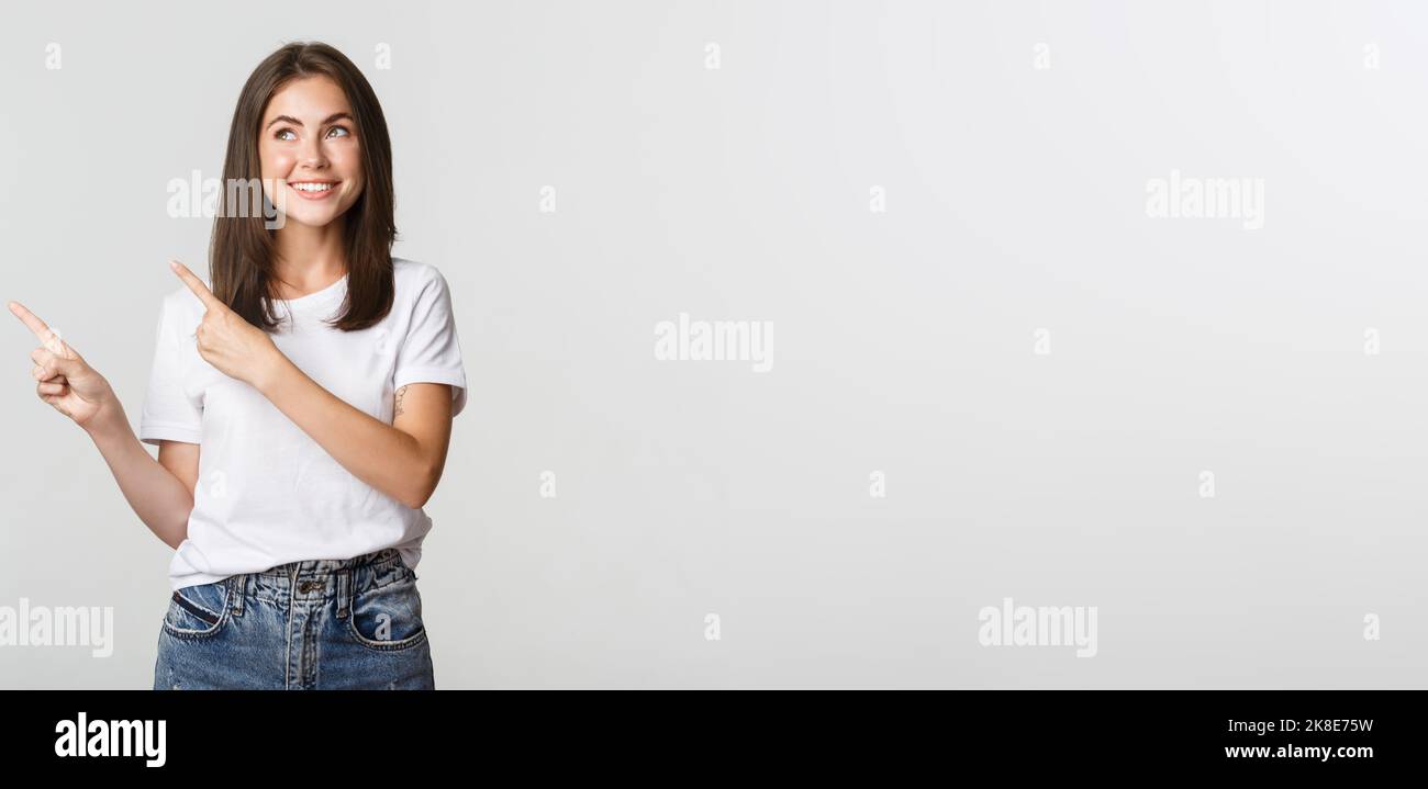 Dreamy beautiful girl smiling, pointing fingers upper left corner and ...