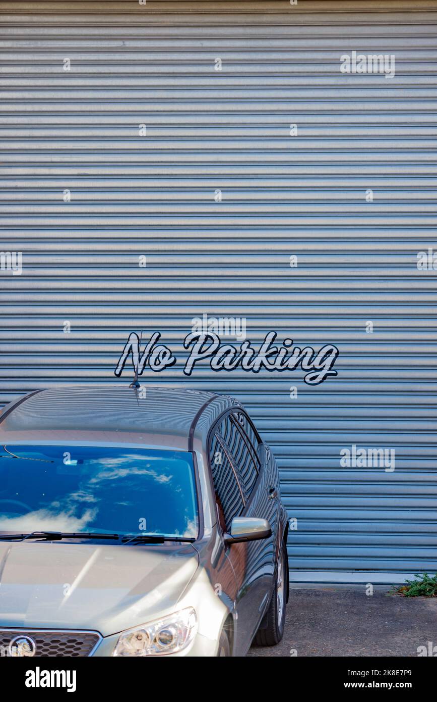 No Parking sign painted on a roller door wit ha car parked directly in ...