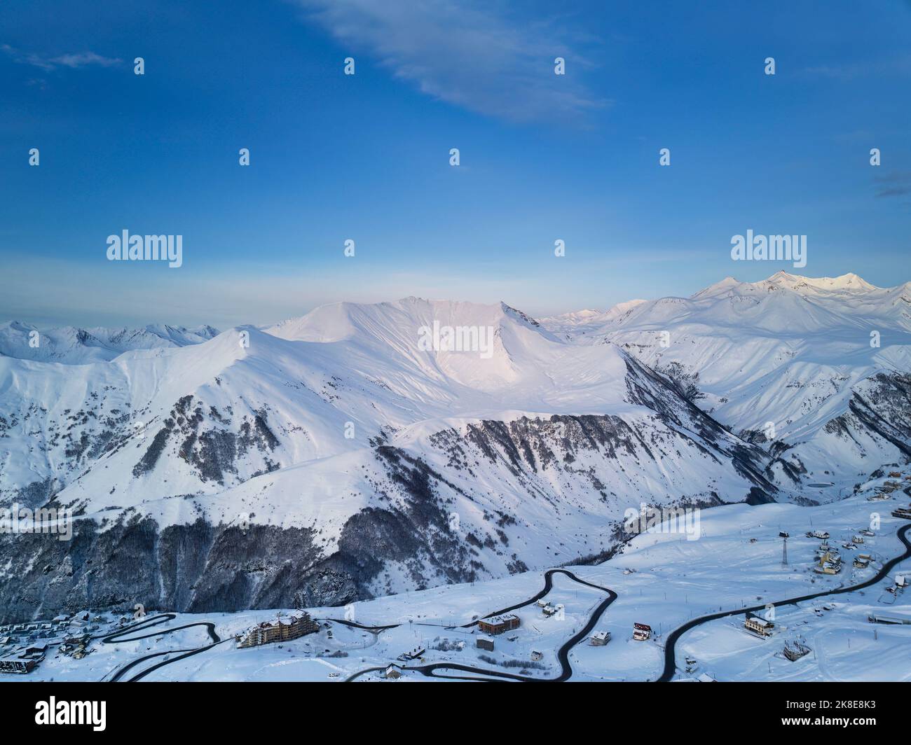 Wide aerial panorama of snowy mountain ridge at ski resort village on ...