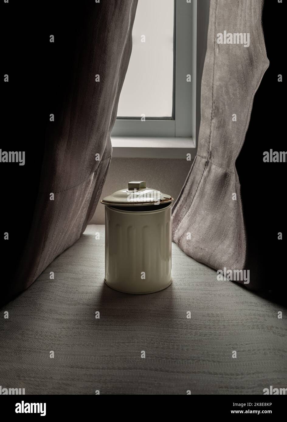 Yellow steel trash can with open lid on the window cushions seat of the ...