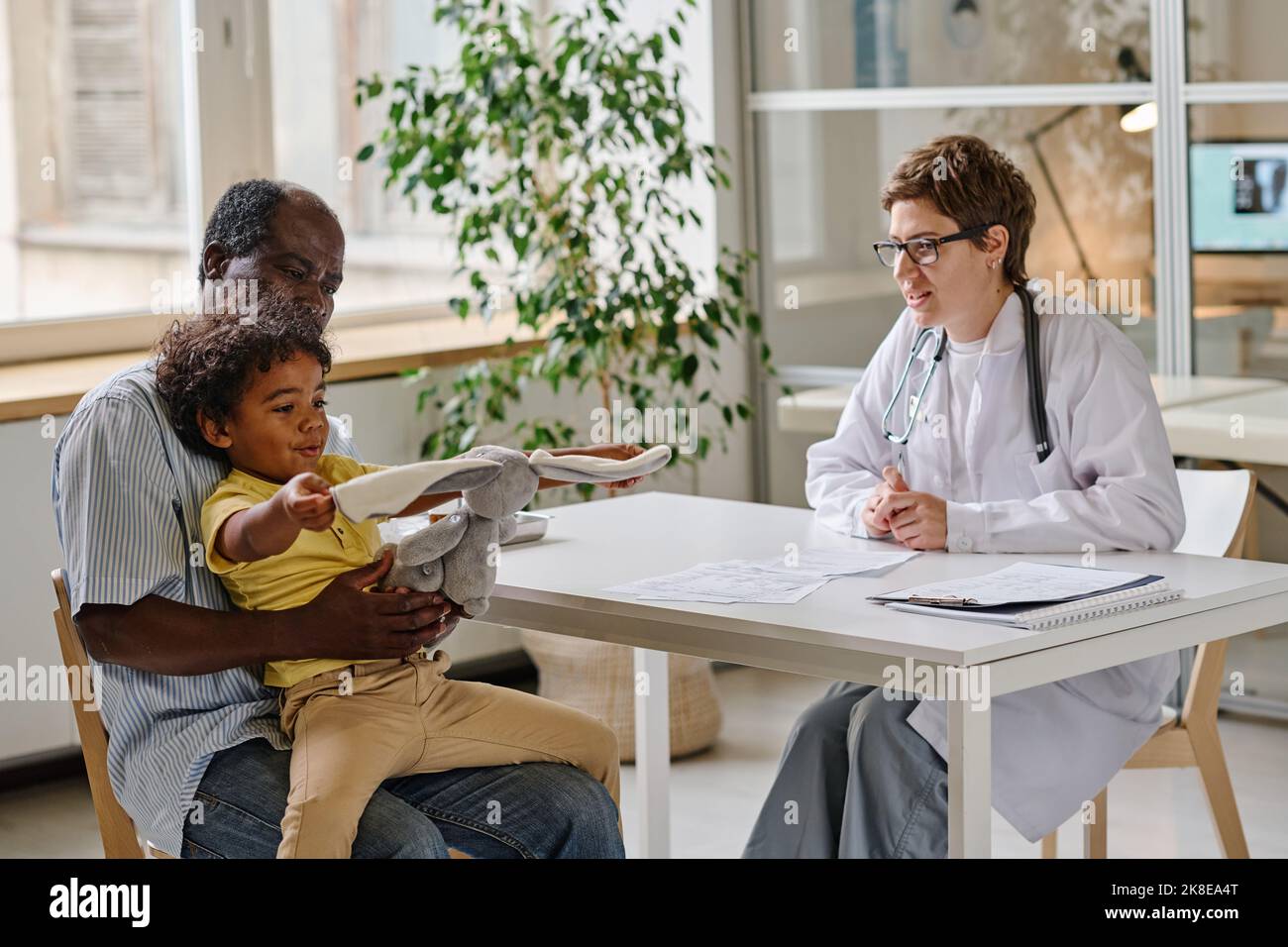 Female doctor talking to little patient at table while they visiting ...