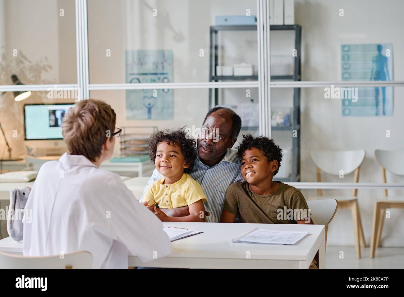 African dad with his two sons tlking to doctor while they sitting at ...