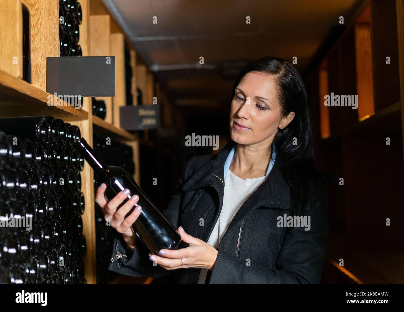 Woman in the wine cellar with bottles in background drinking and ...