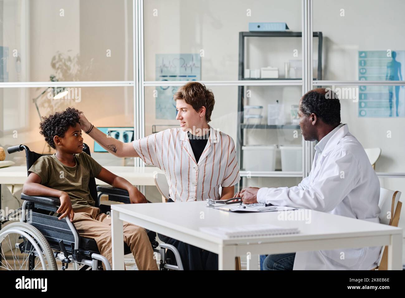 African boy in wheelchair visiting doctor with his mom, they discussing ...