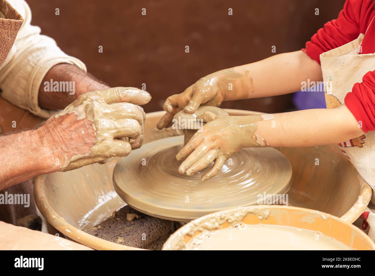 closeup in horizontal view of the hands of a potter and a girl while ...