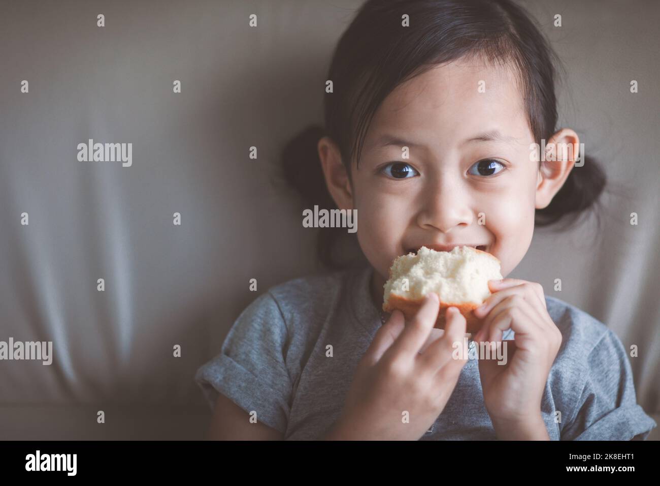 Bright-eyed Asian girl happily eating bread.Children concept with ...