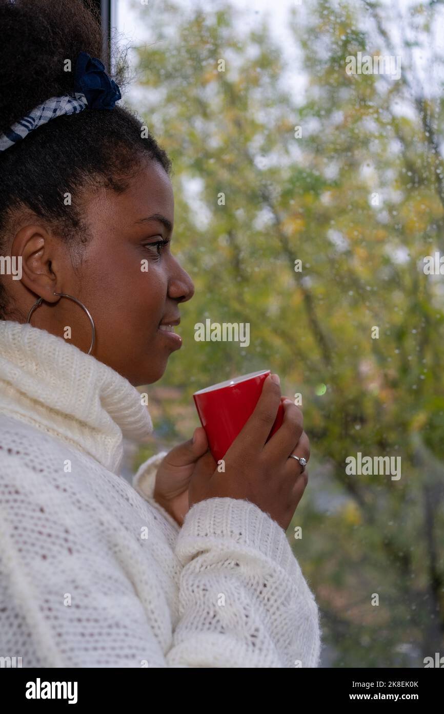 Young African American woman drinking coffee looking out the window on ...
