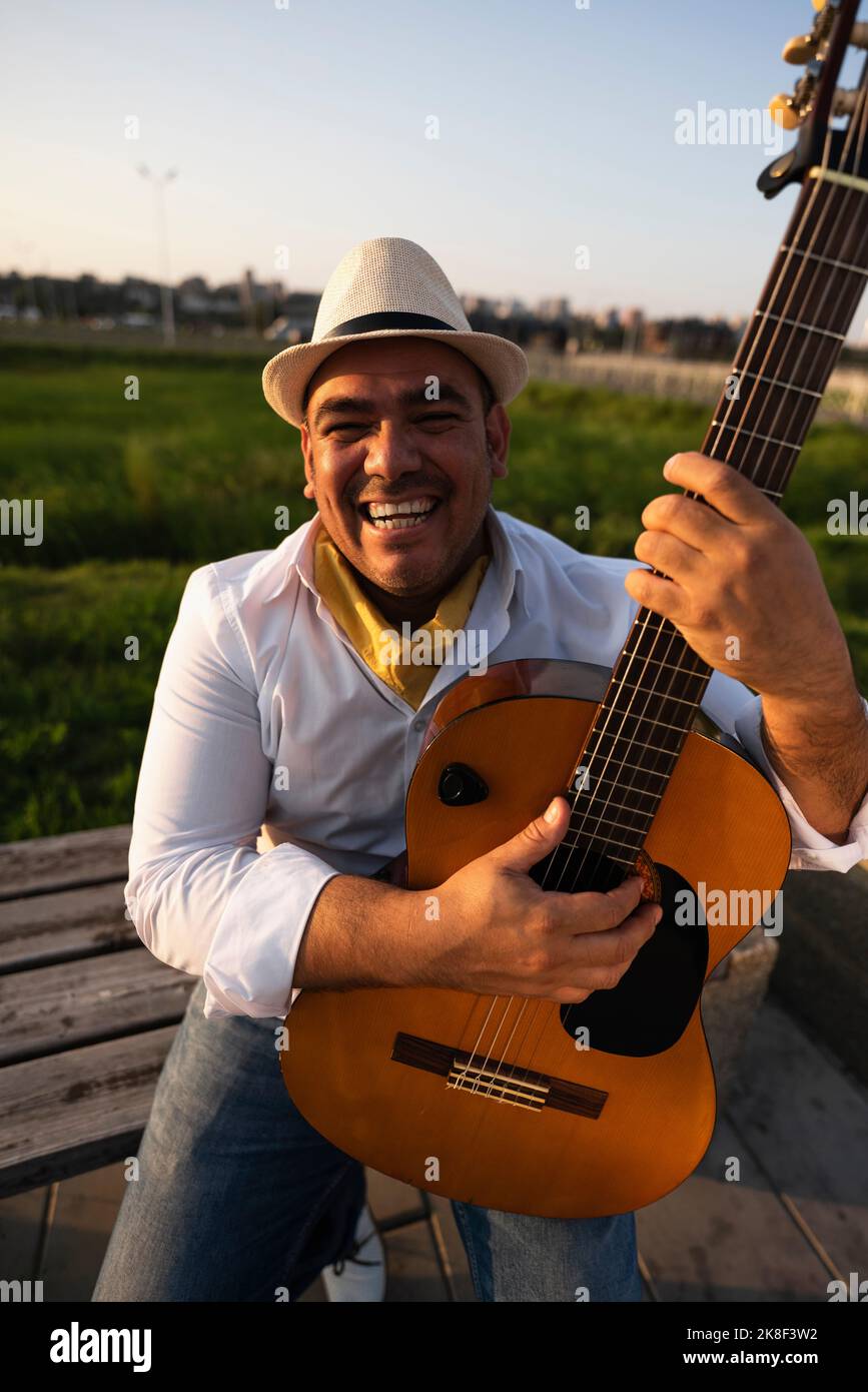 Happy guitarist holding guitar on bench Stock Photo - Alamy