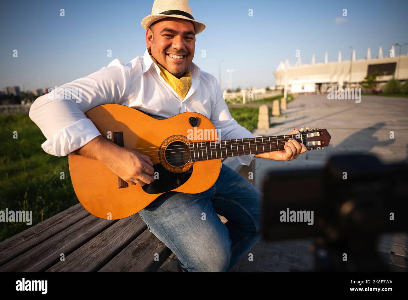 Smiling guitarist playing guitar and recording through smart phone on ...