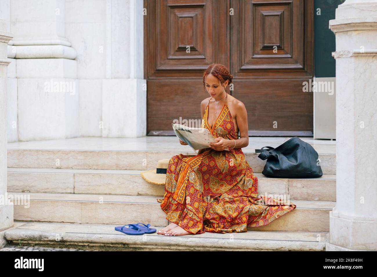 Young woman with curly hair reading map sitting on steps Stock Photo ...
