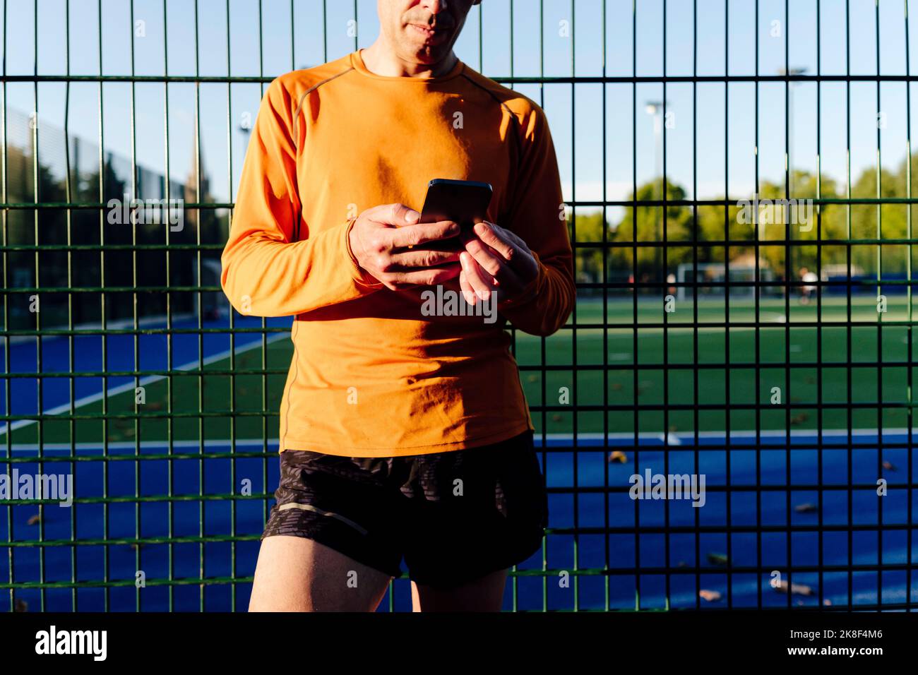 Sportsman holding mobile phone in front of fence Stock Photo - Alamy