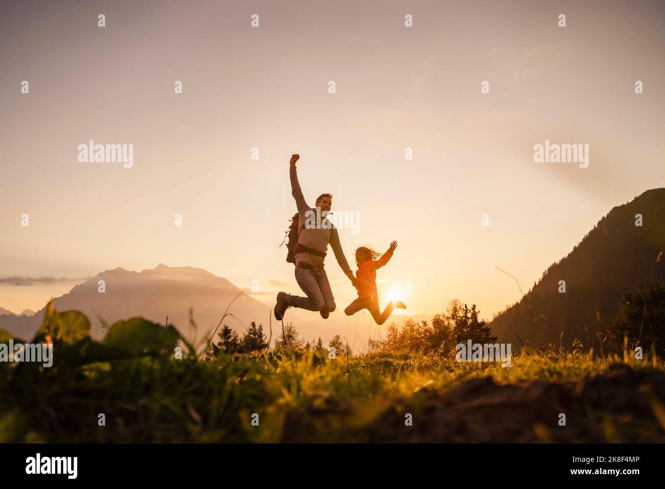 Happy man with daughter jumping on top of mountain Stock Photo - Alamy