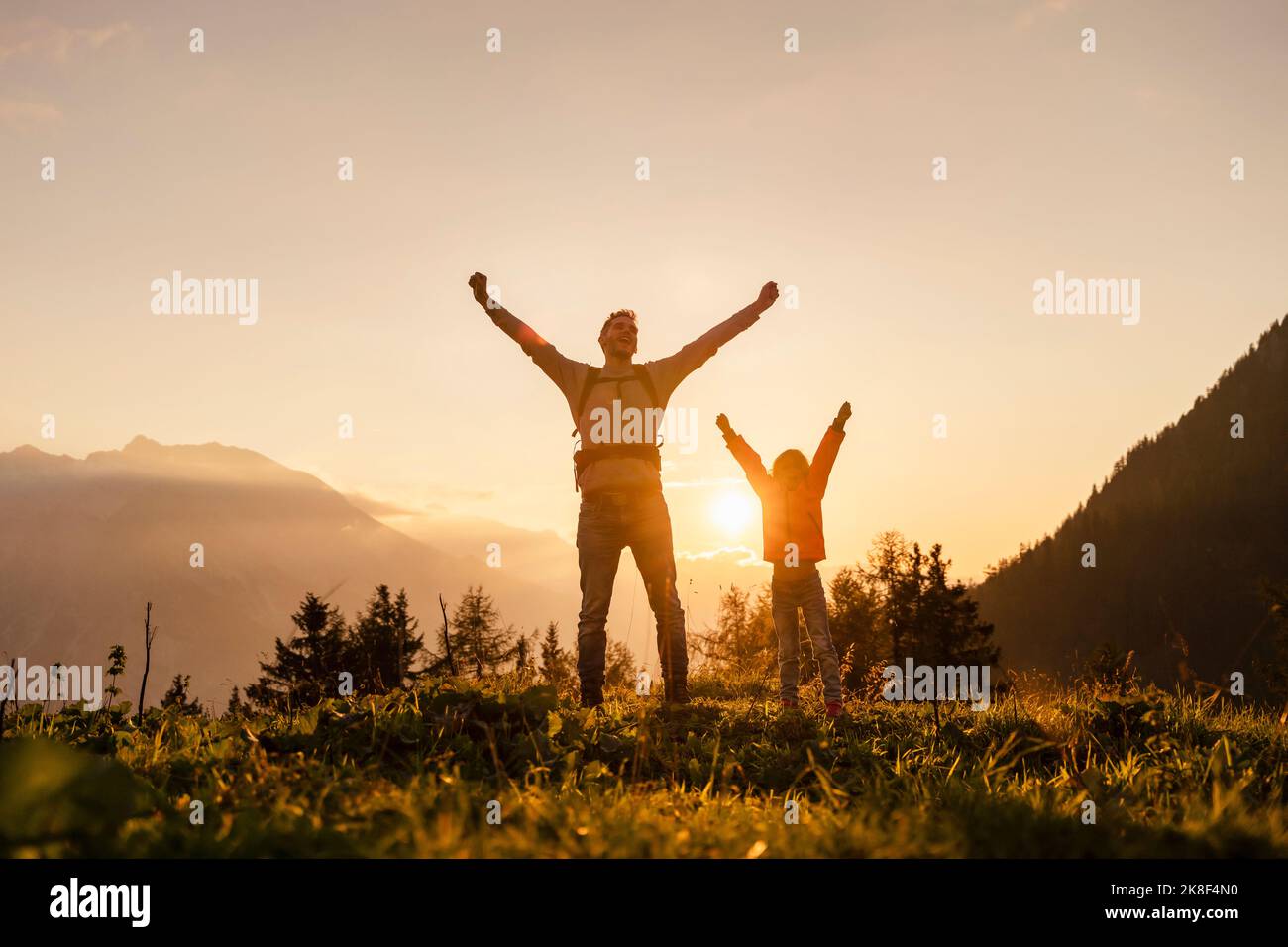 Man with daughter rising fist on top of mountain at sunset Stock Photo ...