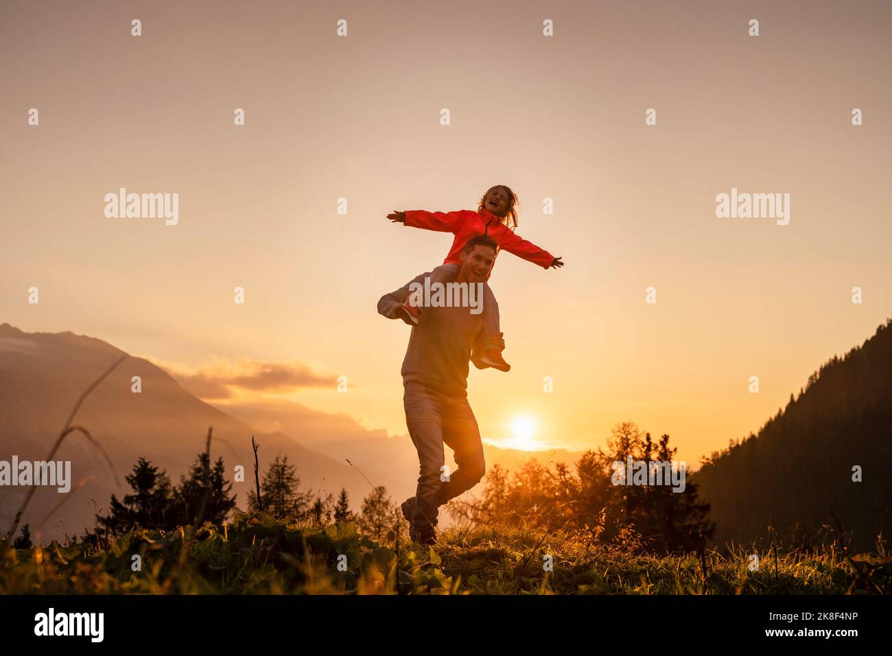 Playful mature man carrying daughter with arms outstretched running on ...