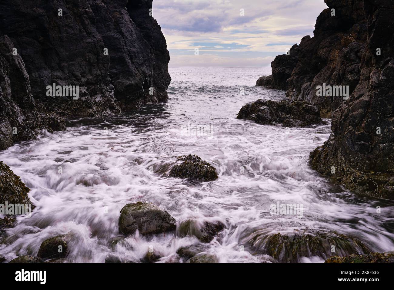 Waves breaking as they enter a rocky cove and swirling over the rocks ...