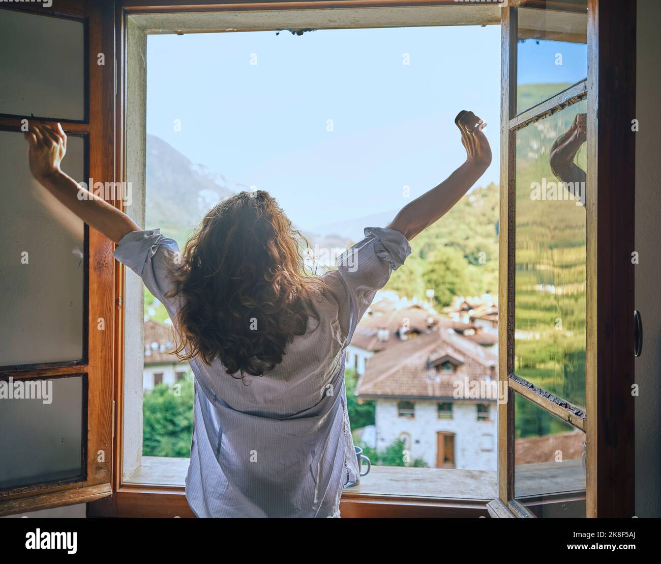 Mature woman stretching with arms raised looking out through window ...